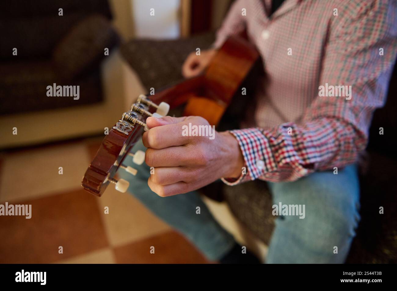 A close-up view of a person adjusting the tuning peg of a guitar while ...