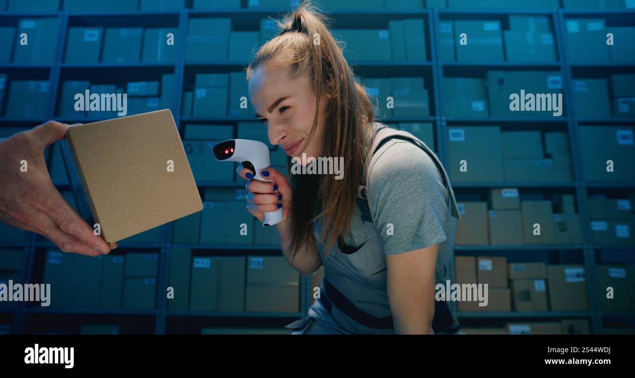 Positive Female Warehouse Worker Looking at Camera, Scanning Cardboard ...