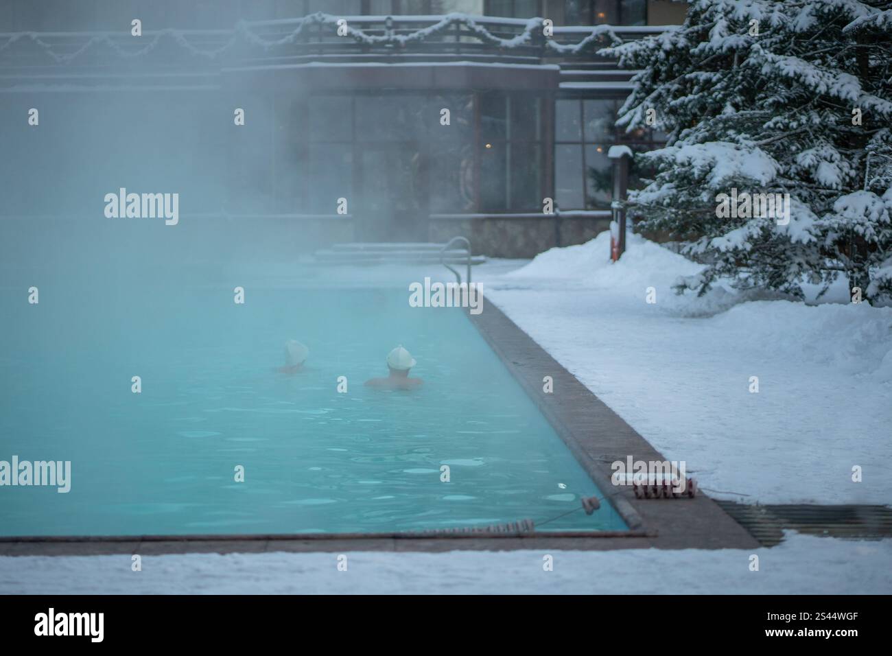 People swimming in outdoor pool with warm water in cold weather. Winter ...