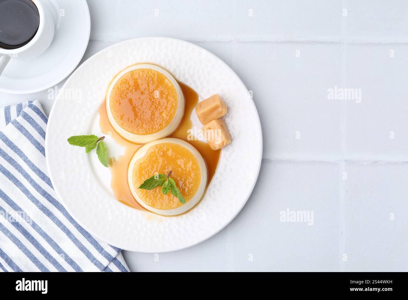 Tasty puddings with caramel sauce served on white tiled table, top view ...