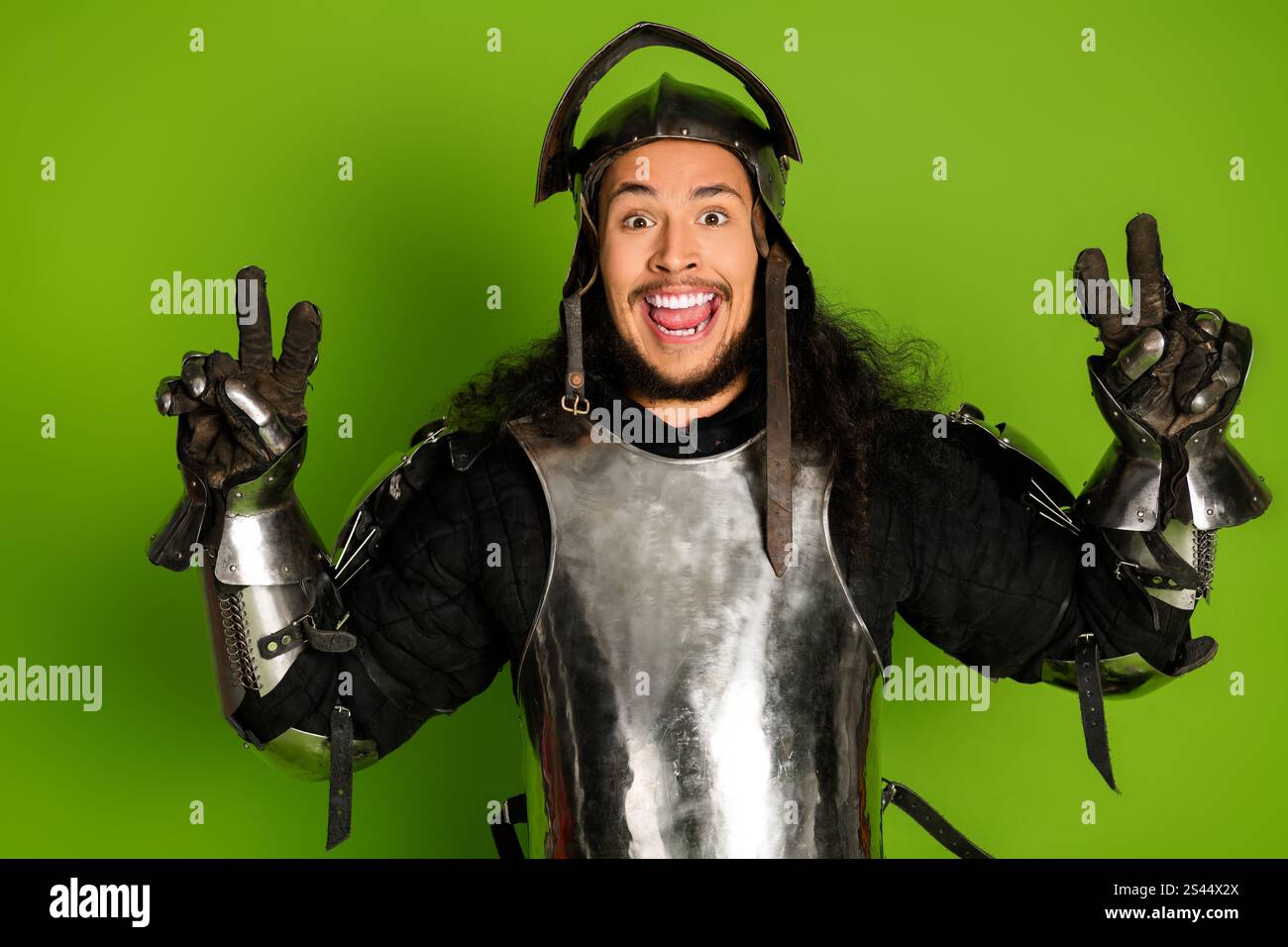 Funny young man in medieval knight armor posing with a green background ...