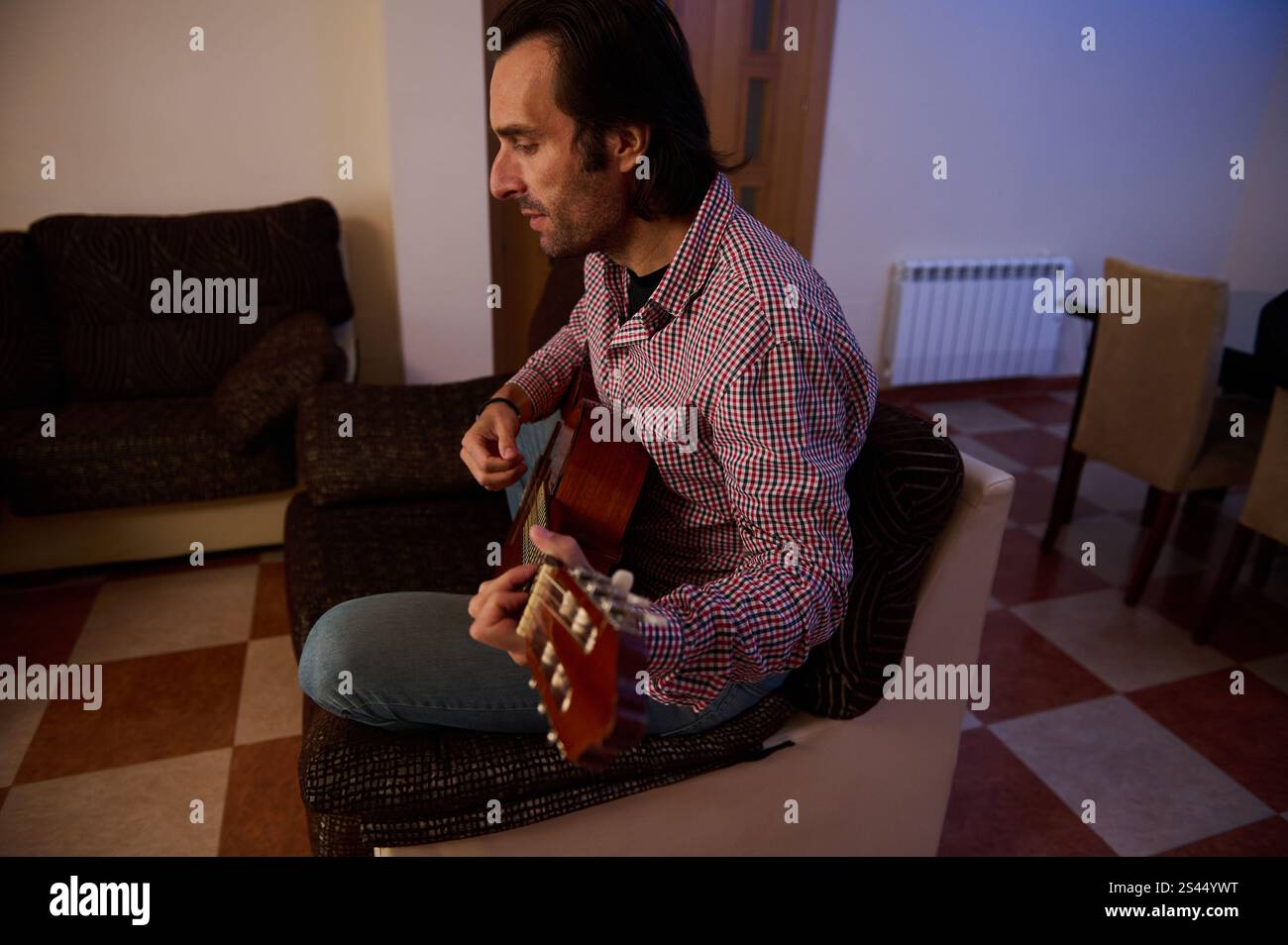 A person playing an acoustic guitar while seated on a couch in a ...