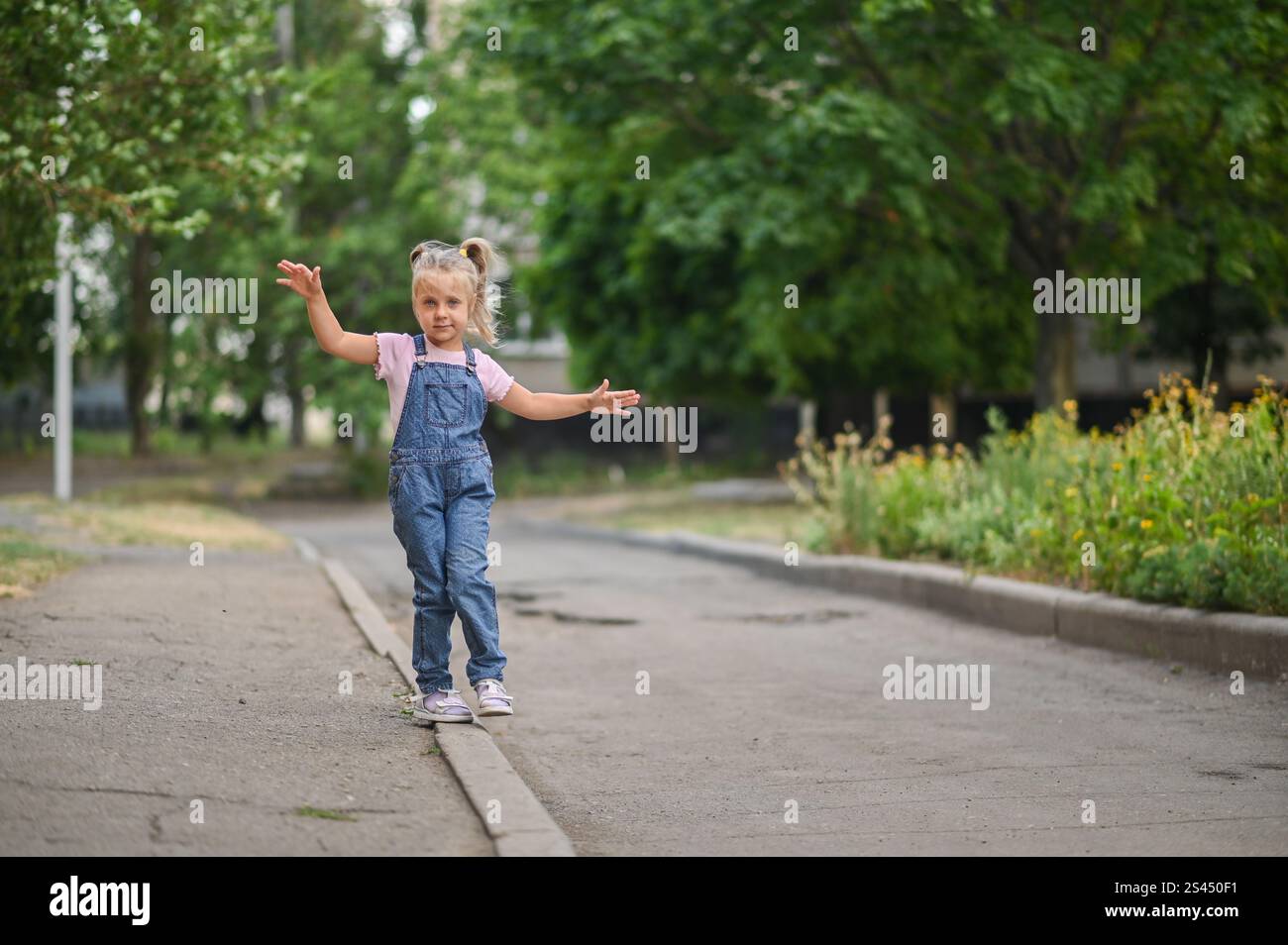 The girl walks along the sidewalk, keeping her balance, arms ...