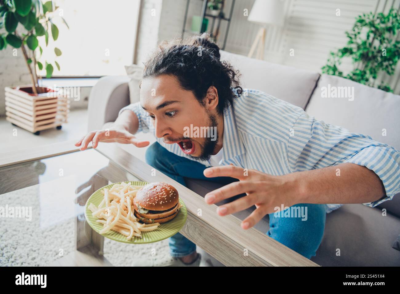 Young man excitedly reaching for a hamburger and fries in a cozy living ...