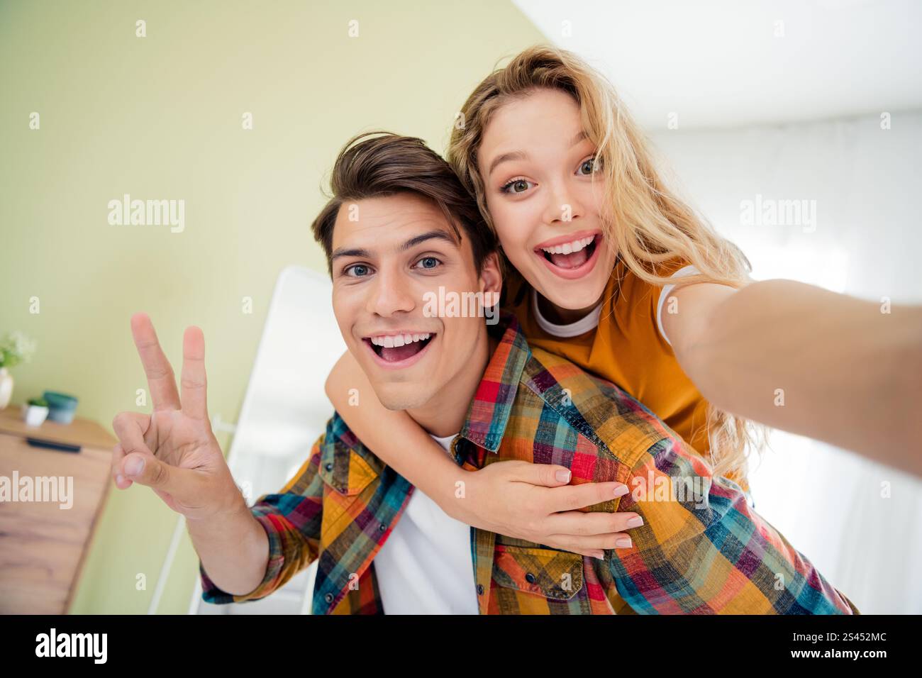 Cheerful young couple capturing a fun indoor moment with peace sign and ...