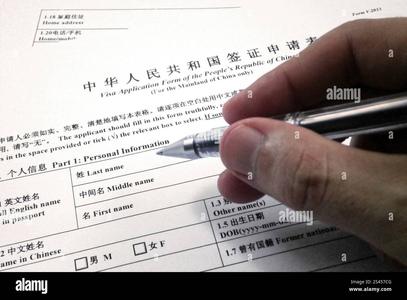 A ballpoint pen held by the fingers of a man filling a visa application ...