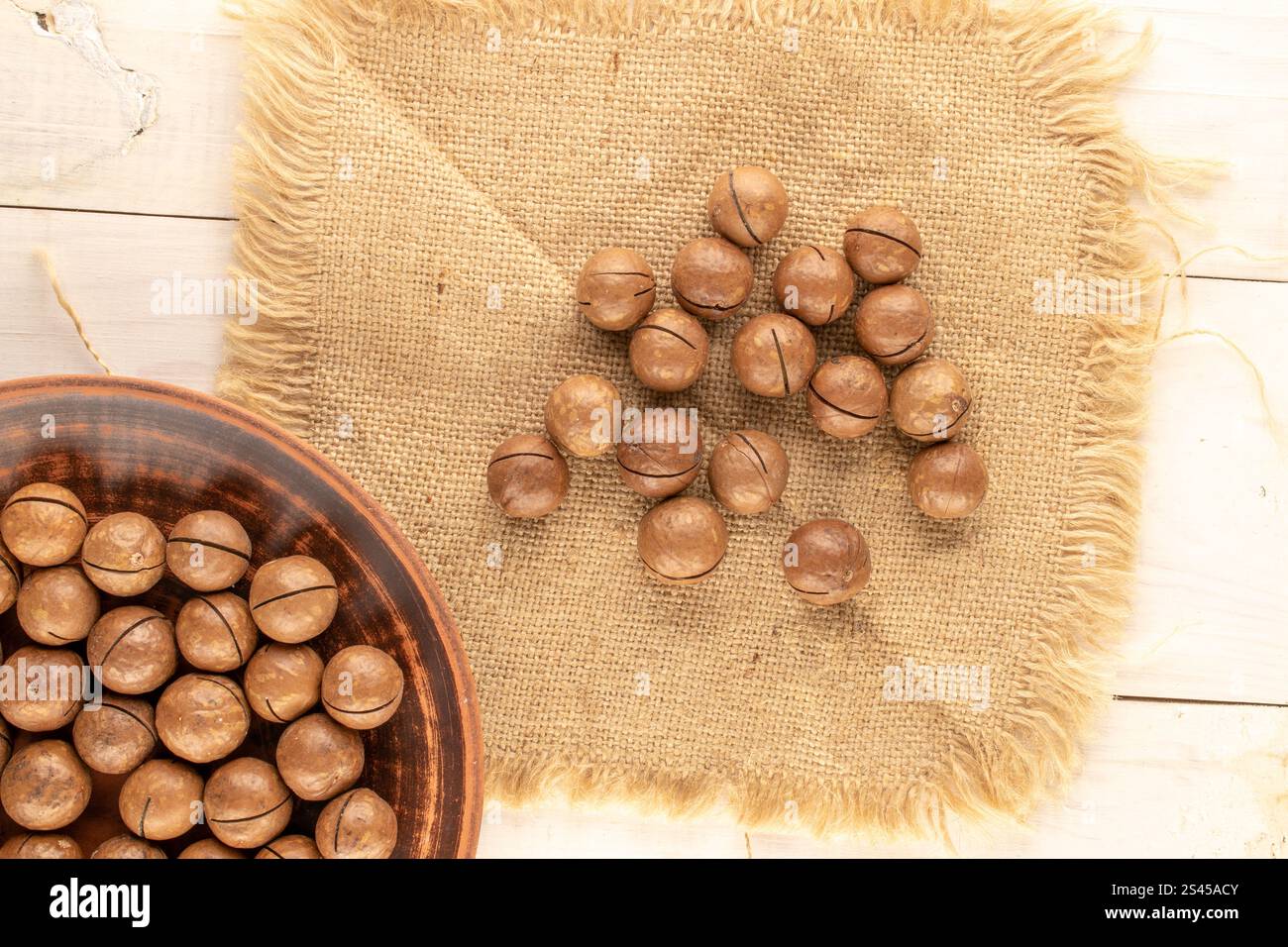 Macadamia nuts in shell with clay plate and jute napkin on wooden table ...