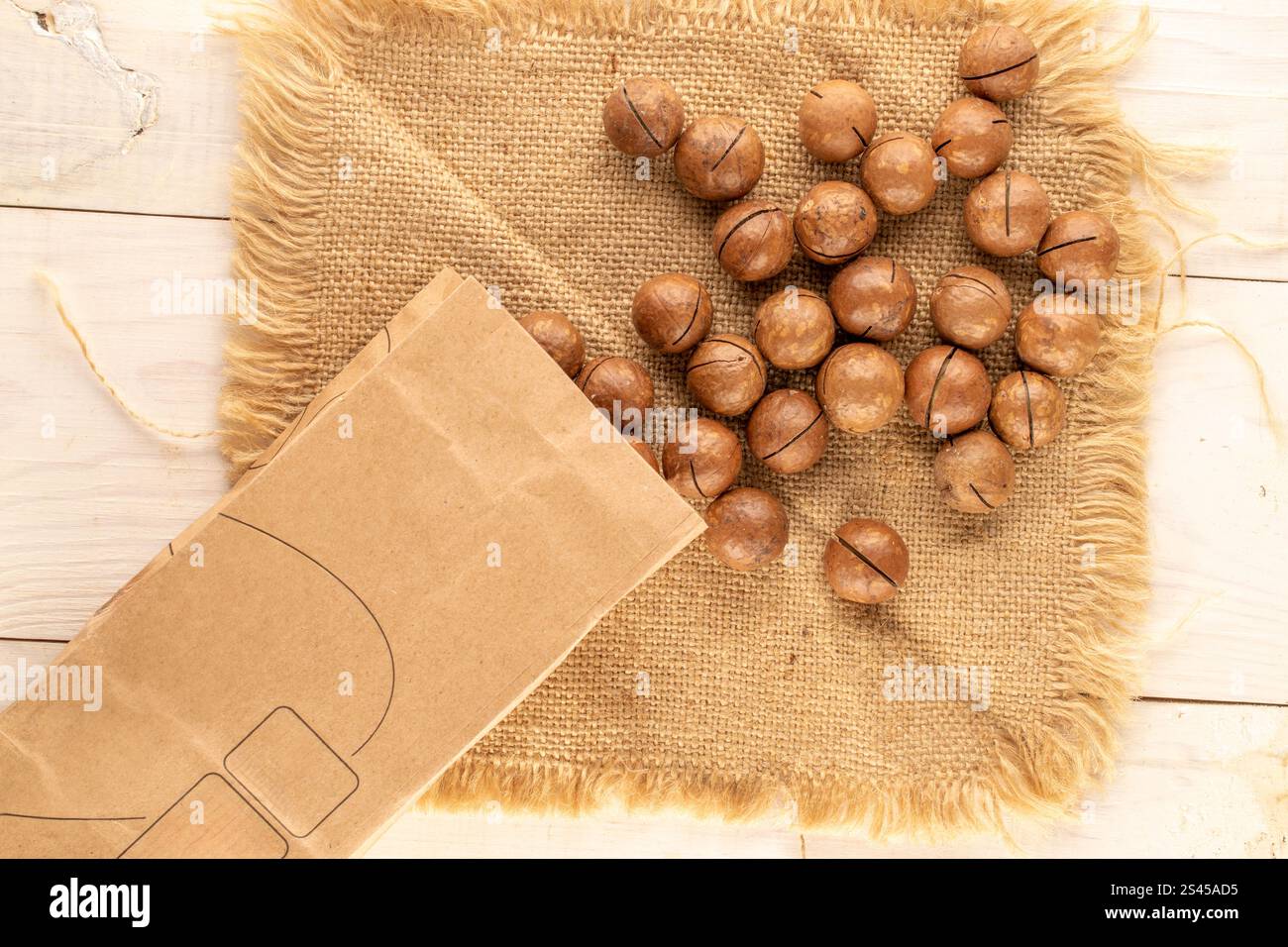 Macadamia nuts in shell with paper bag and jute napkin on wooden table ...