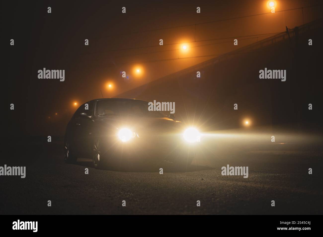 Car headlights though thick fog on an empty city street at night. Dark ...