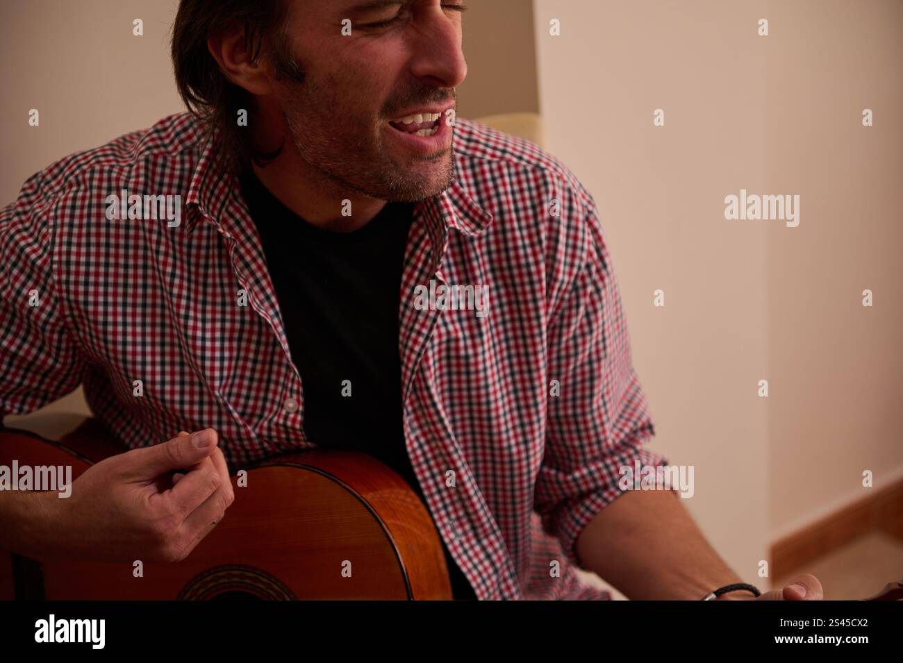 A close-up of a man intensely playing an acoustic guitar indoors ...