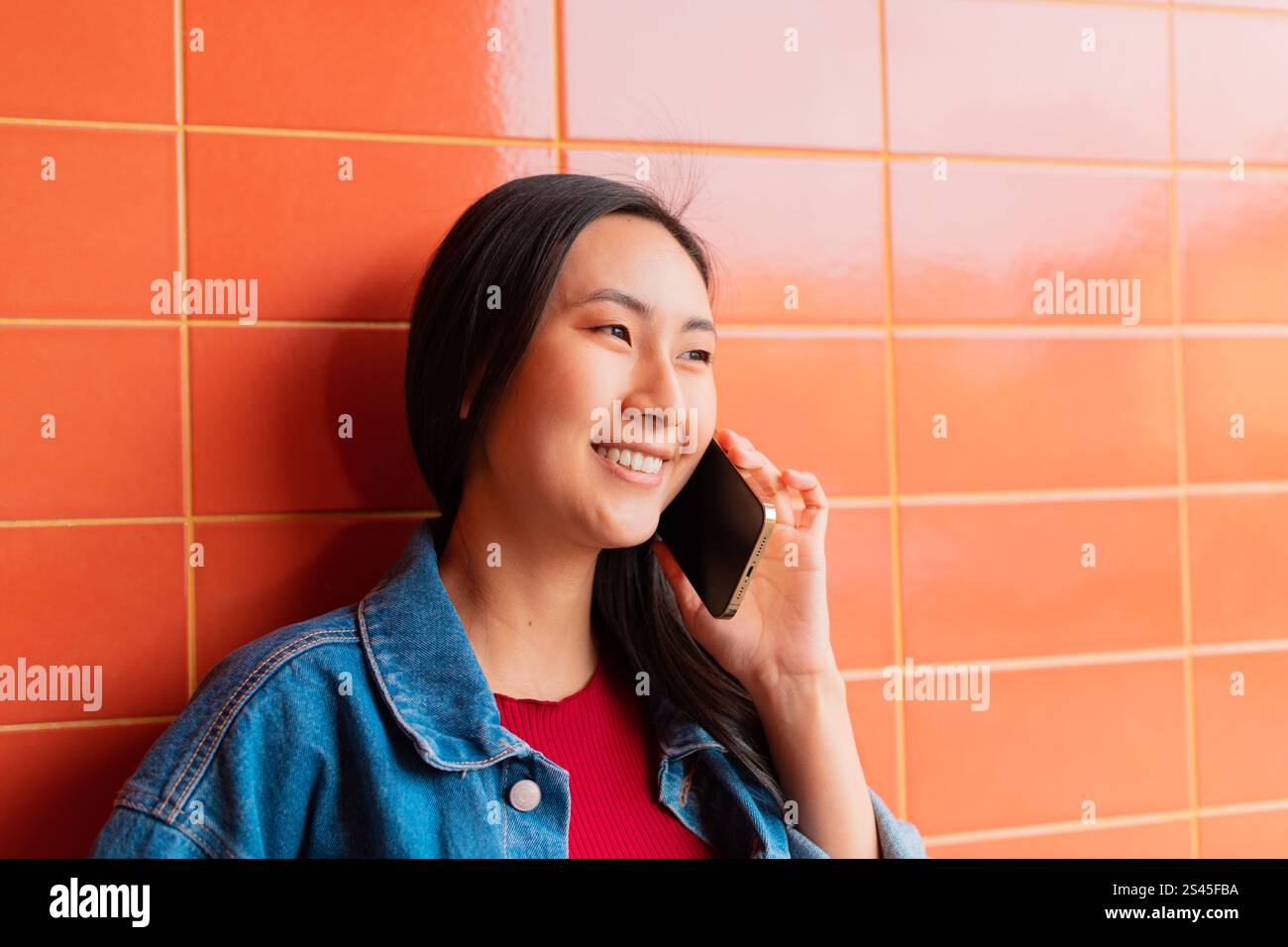 Asian young woman talking on smartphone standing on a red brick wall ...
