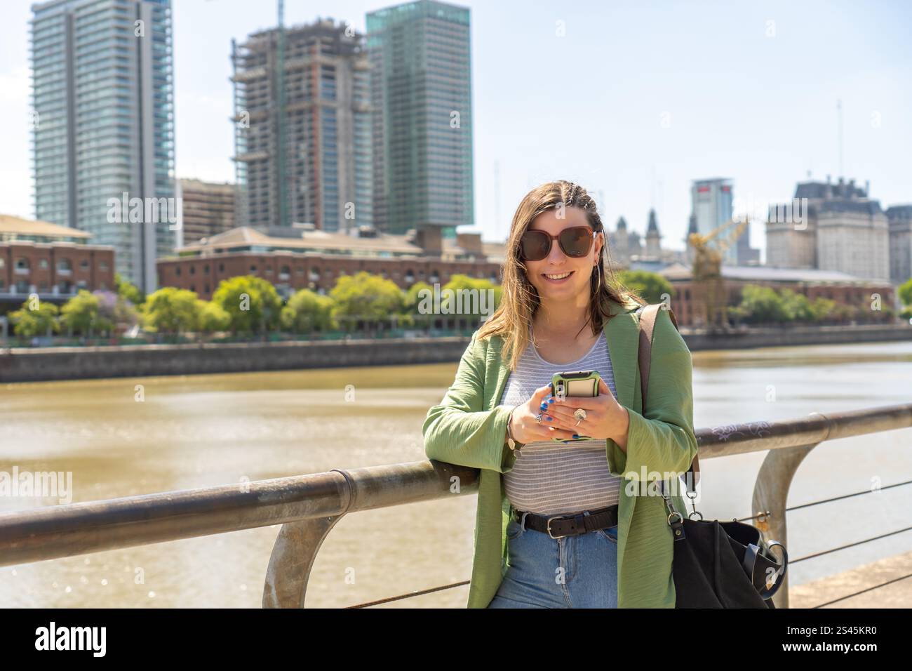 A cheerful woman wearing sunglasses and a green jacket leans on a ...