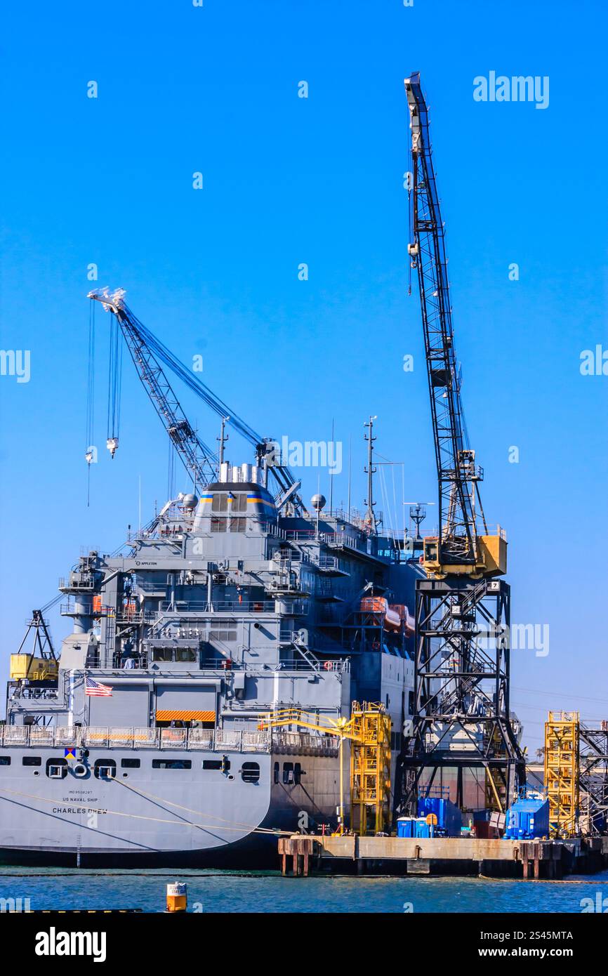 A large ship is docked at a pier with a crane lifting a large object ...