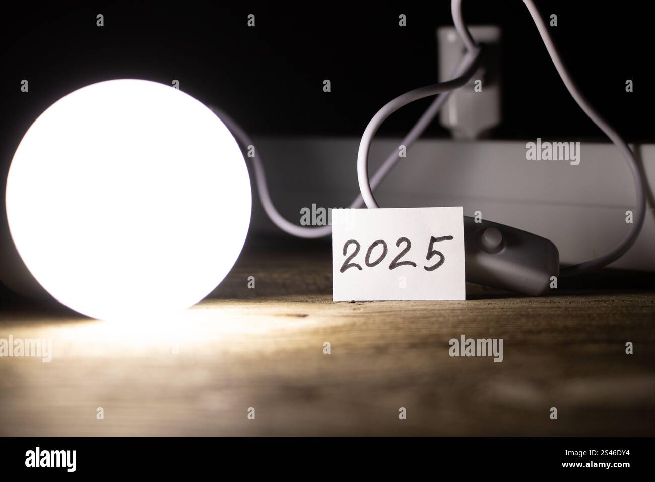 An energy saving light bulb is on a wooden floor near a socket and a ...