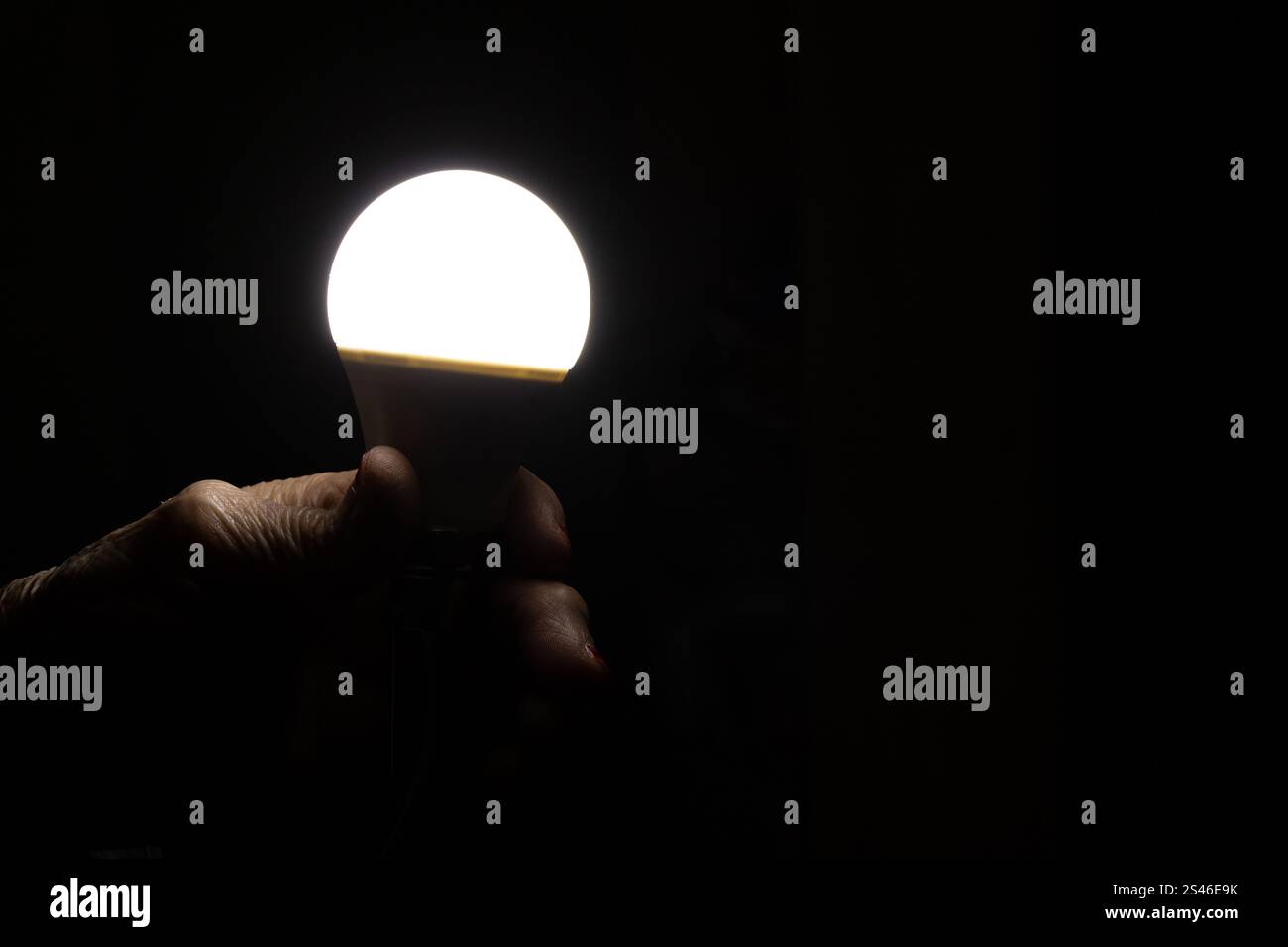 Energy saving light bulb in hand of elderly woman in dark room, lamp ...