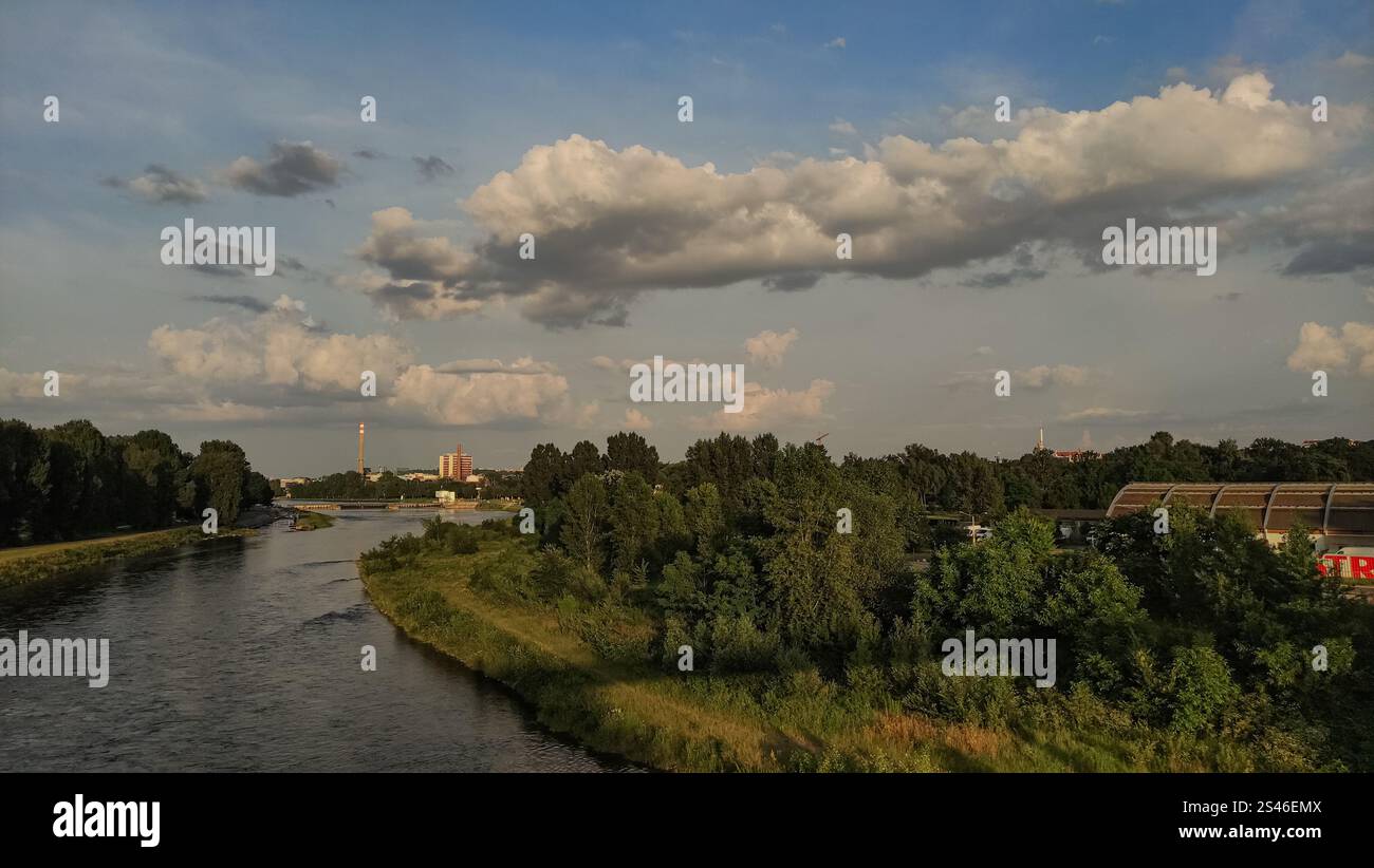 A river flows through a green forest, with buildings visible in the ...