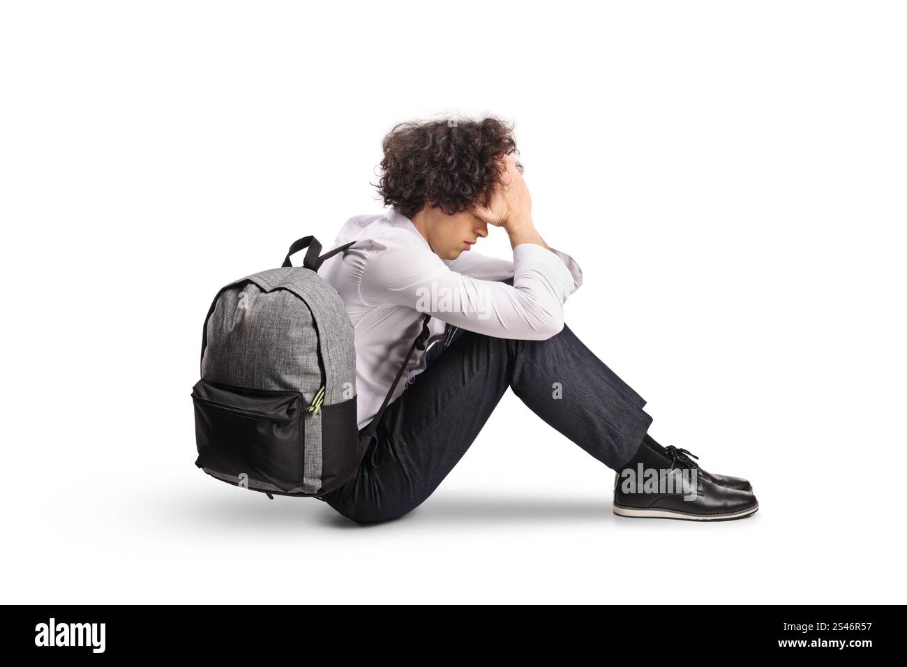 Sad male student with a backpack sitting on the ground isolated on ...