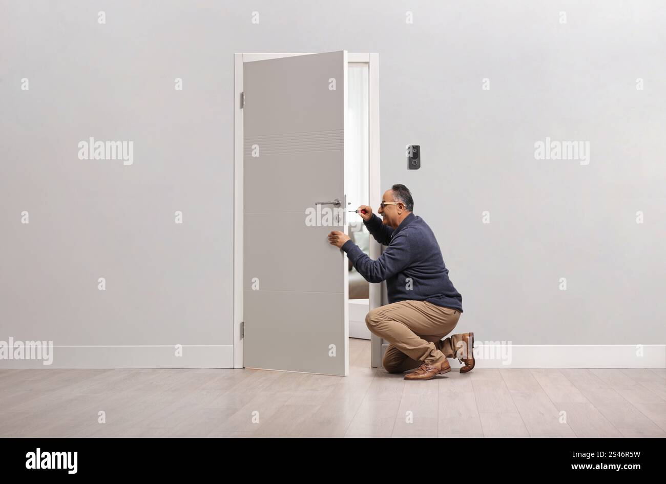 Man kneeling and fixing a door with a screwdriver Stock Photo - Alamy
