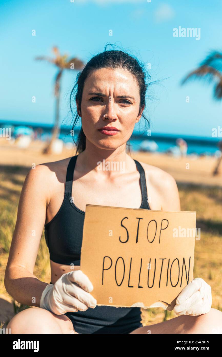 A woman is holding a sign that says "Stop Pollution" while sitting on the beach Stock Photo - Alamy