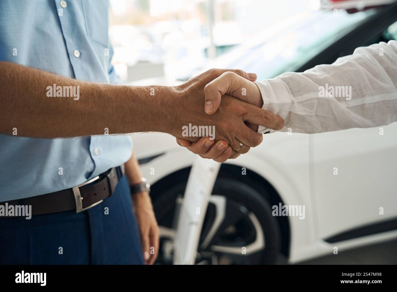Salesman shaking hands with client in modern car dealership Stock Photo ...
