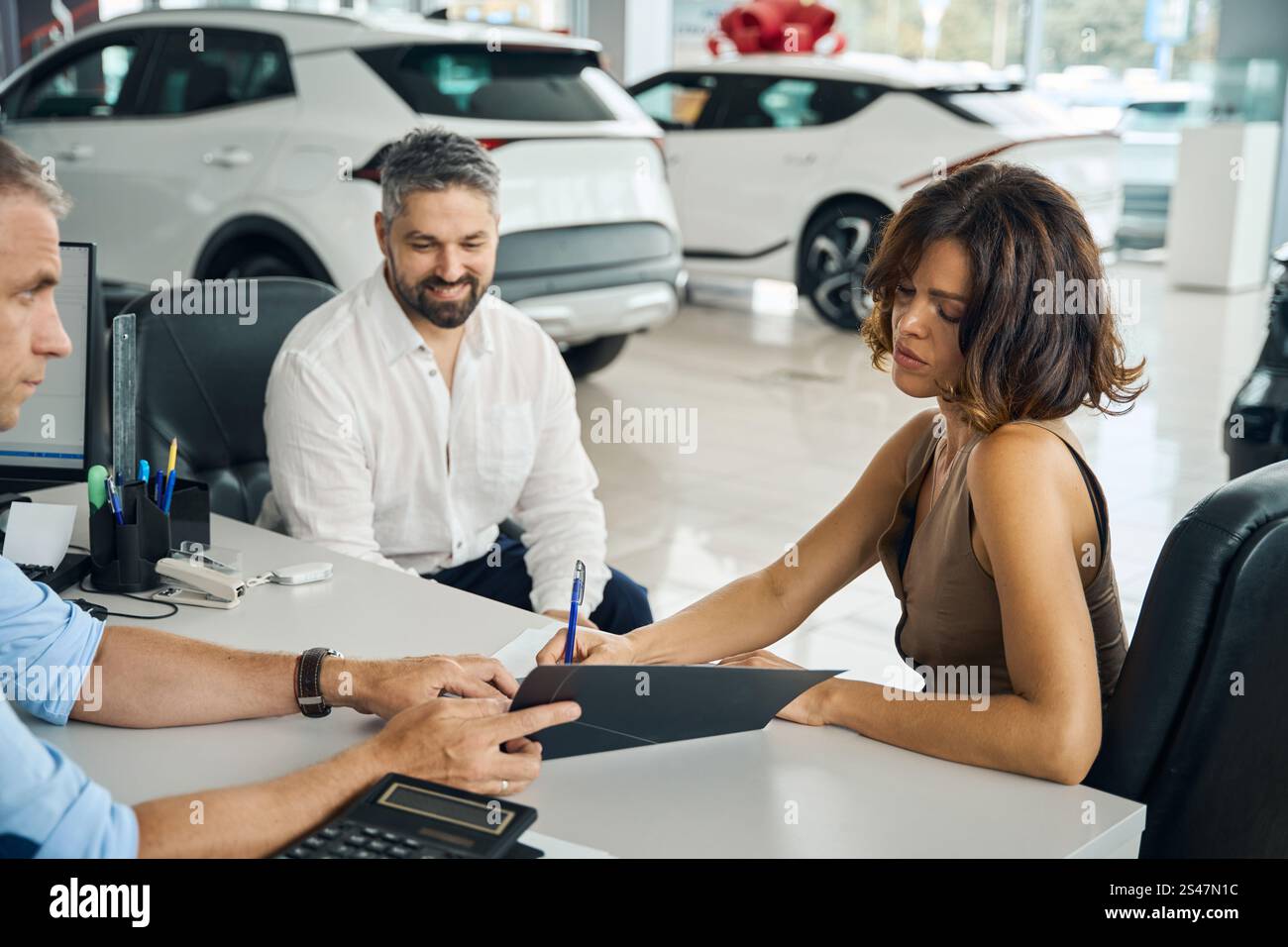 Man and woman buying new car in a car dealership signing documents ...