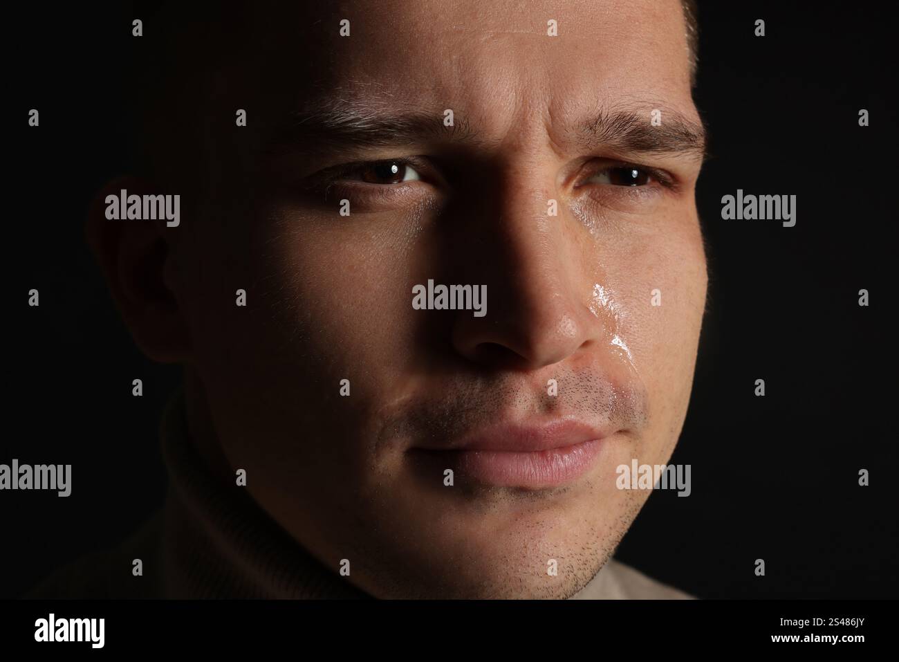 Distressed young man crying on black background, closeup Stock Photo ...