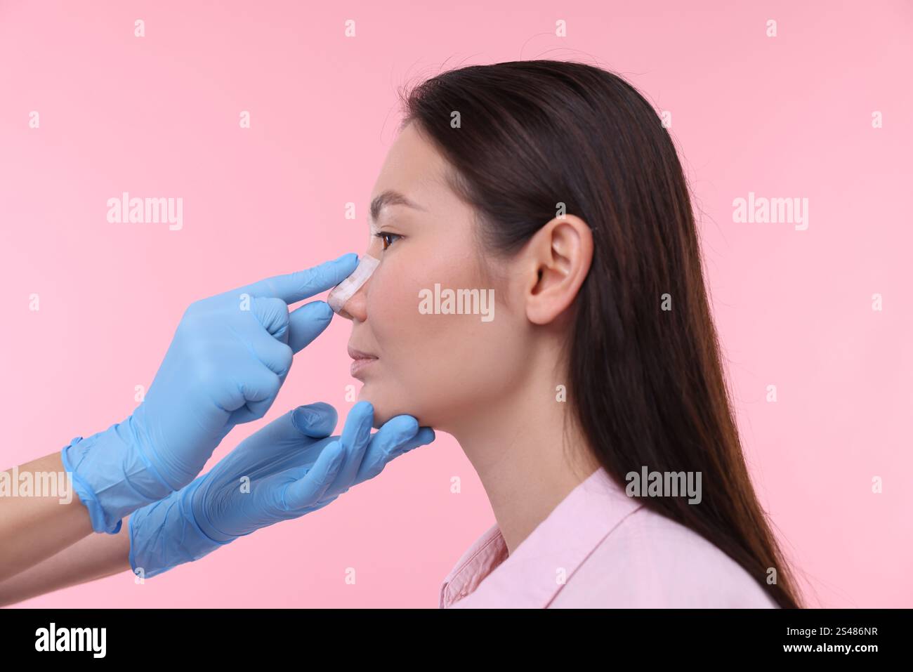 Doctor checking patient's nose after plastic surgery operation on pink ...