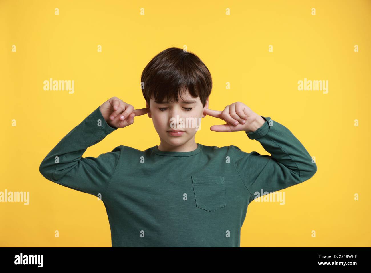 Annoyed boy covering his ears due to loud sound on yellow background ...