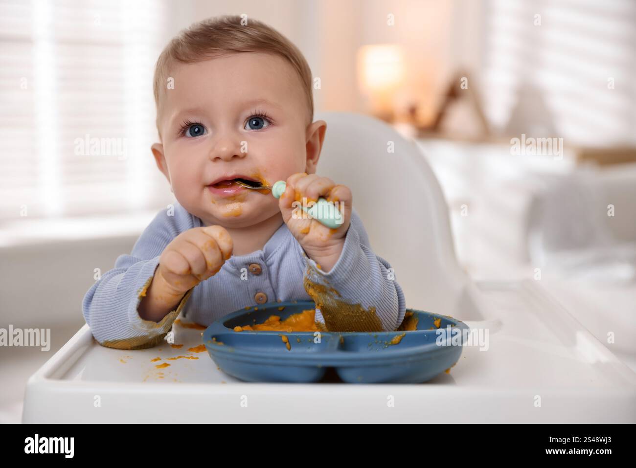 Cute little baby eating healthy food in high chair indoors Stock Photo ...