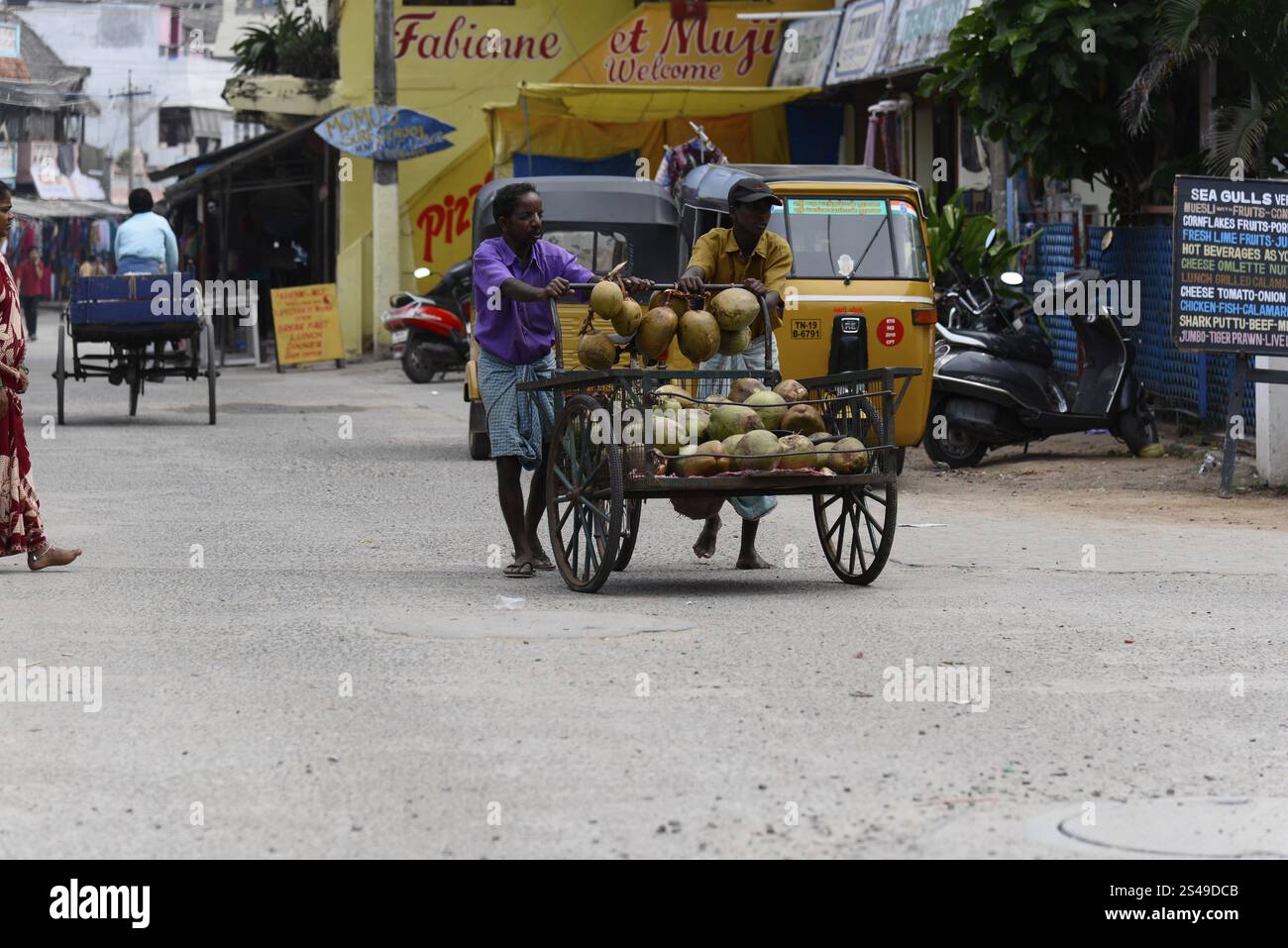 Two men pushing a coconut cart through a busy street, Mahabalipuram ...