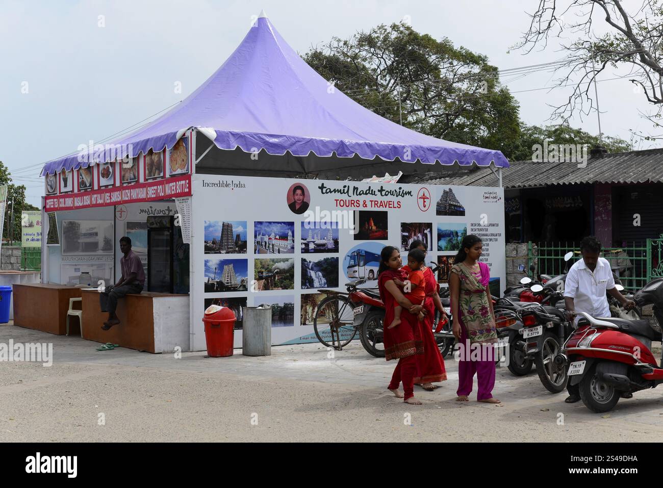 Tourism stall with purple tent and passing people and motorbikes ...
