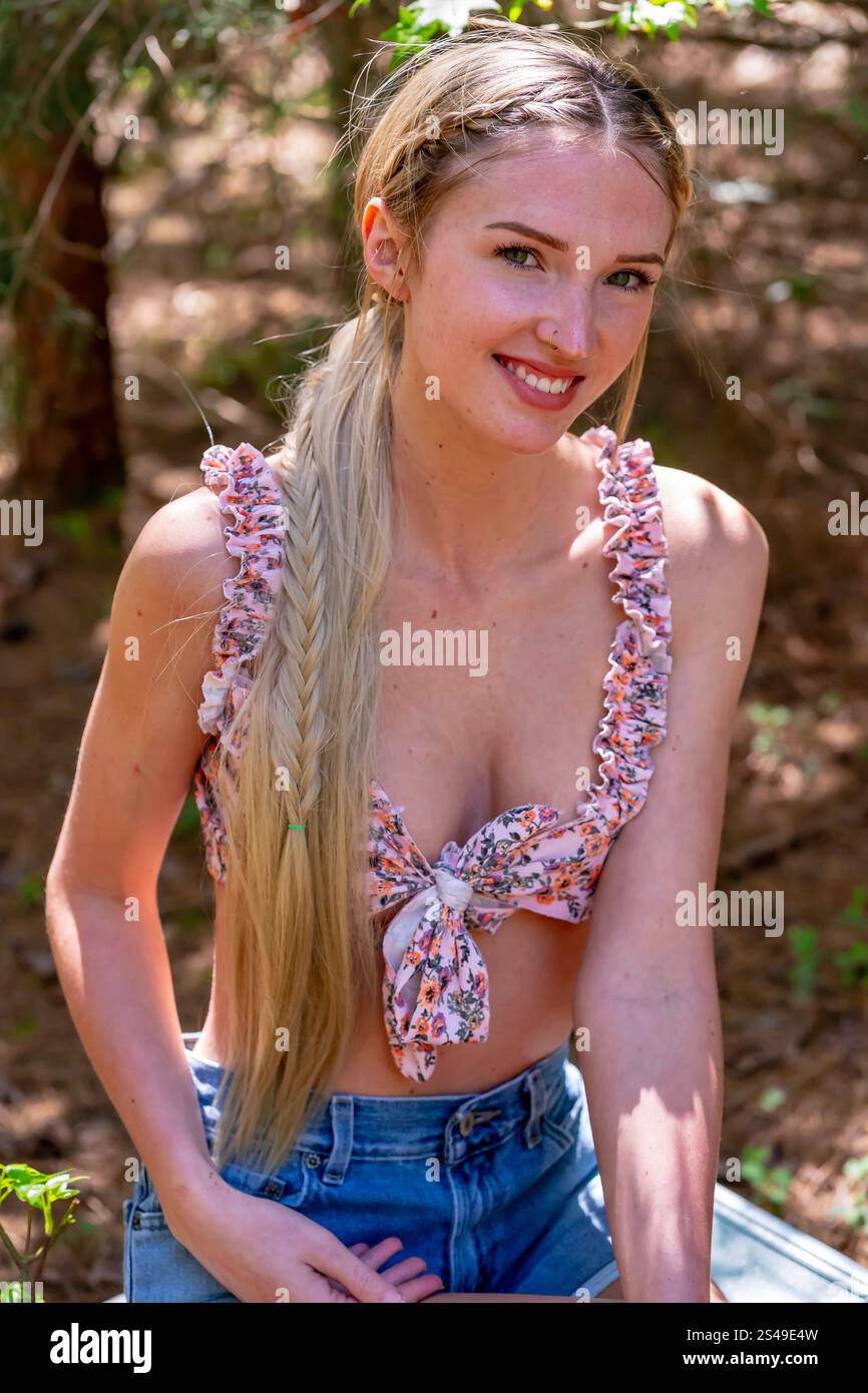 A beautiful young country girl enjoys the summer day on her family farm, basking in sunlight ...