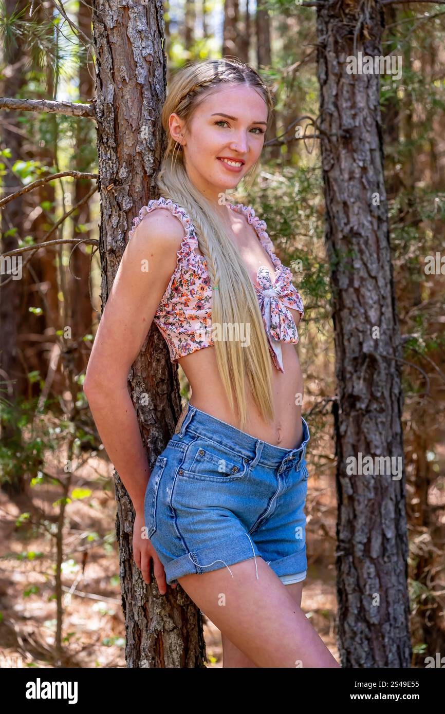 A beautiful young country girl enjoys the summer day on her family farm, basking in sunlight ...
