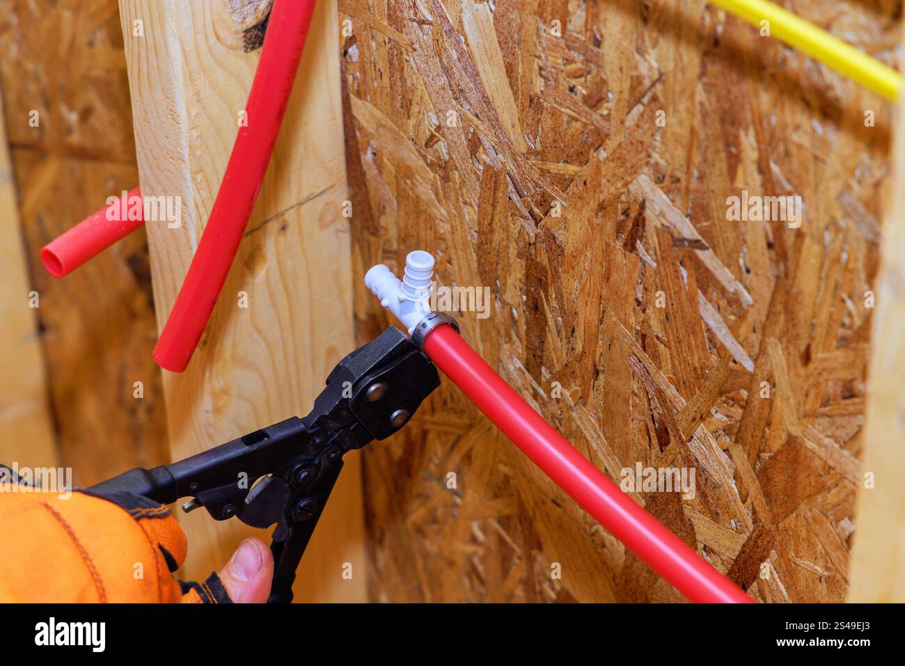 Worker applies pressure with crimping tool to secure red tubing against ...