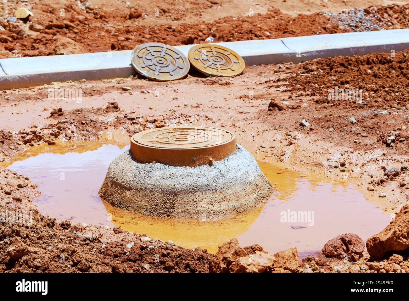 Drainage manhole stands in muddy soil, water, surrounded by ...