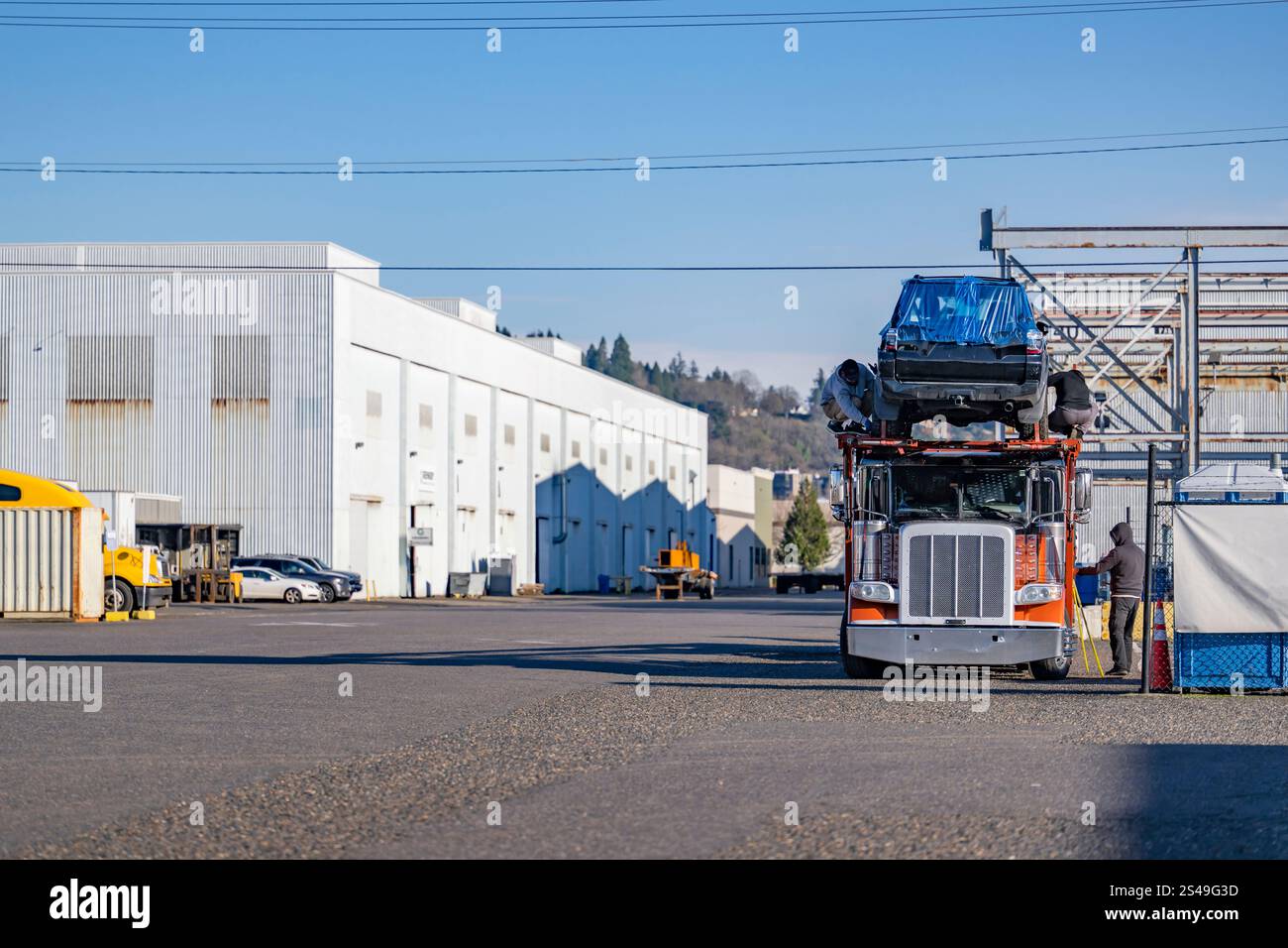 Three workers of the company team fastening covered car on the upper ...