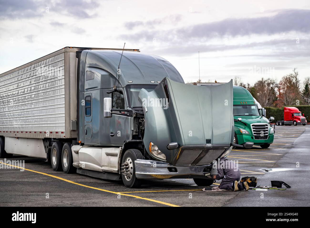 Truck driver repairing broken gray big rig semi truck with open hood ...