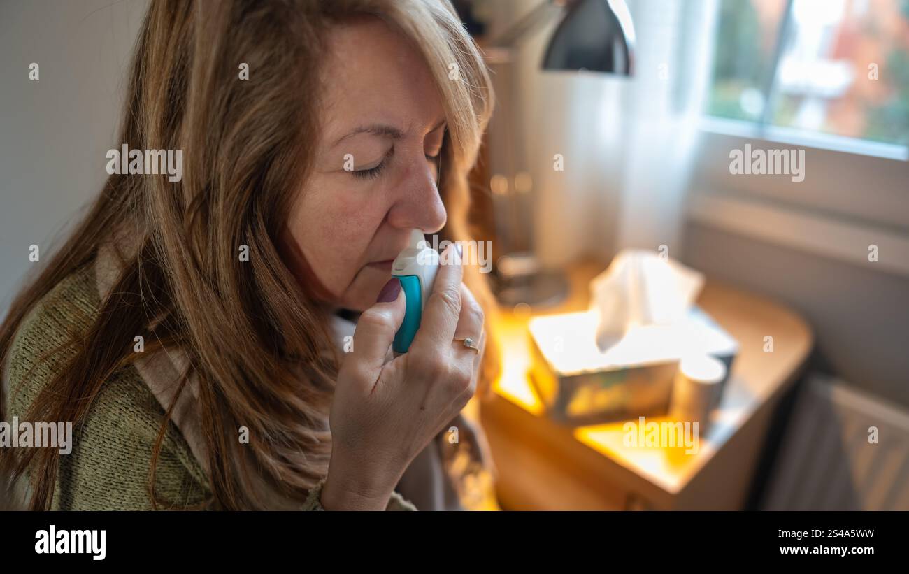 Woman pouring drops with an inhaler into her nose to breathe better from the congestion of the ...