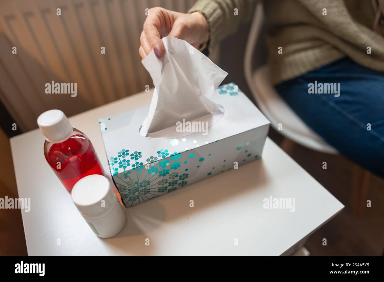 Woman's hand taking tissues from a box and cold medicine on the bedside ...
