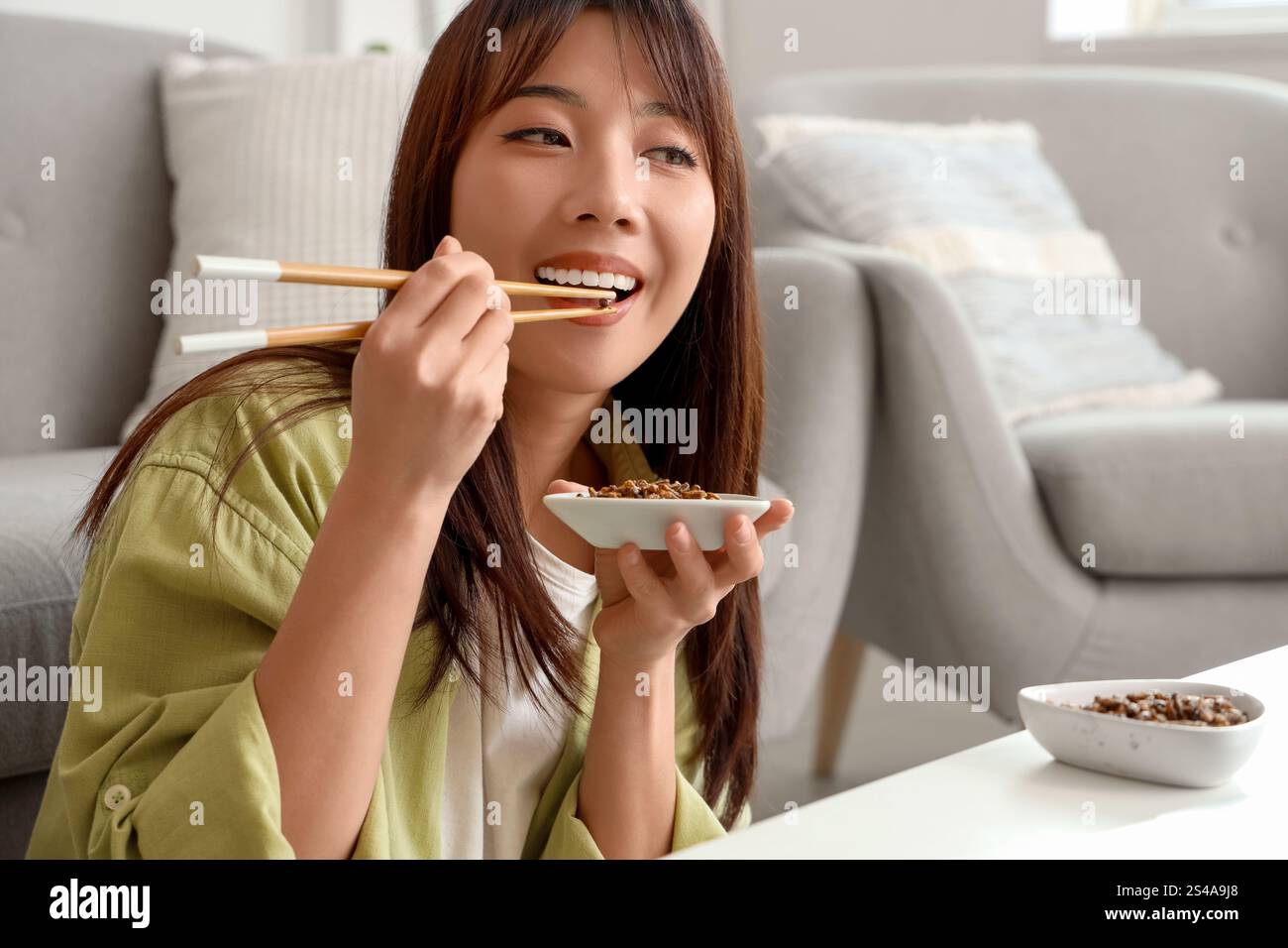 Beautiful Asian woman with chopsticks eating fried insects at home ...