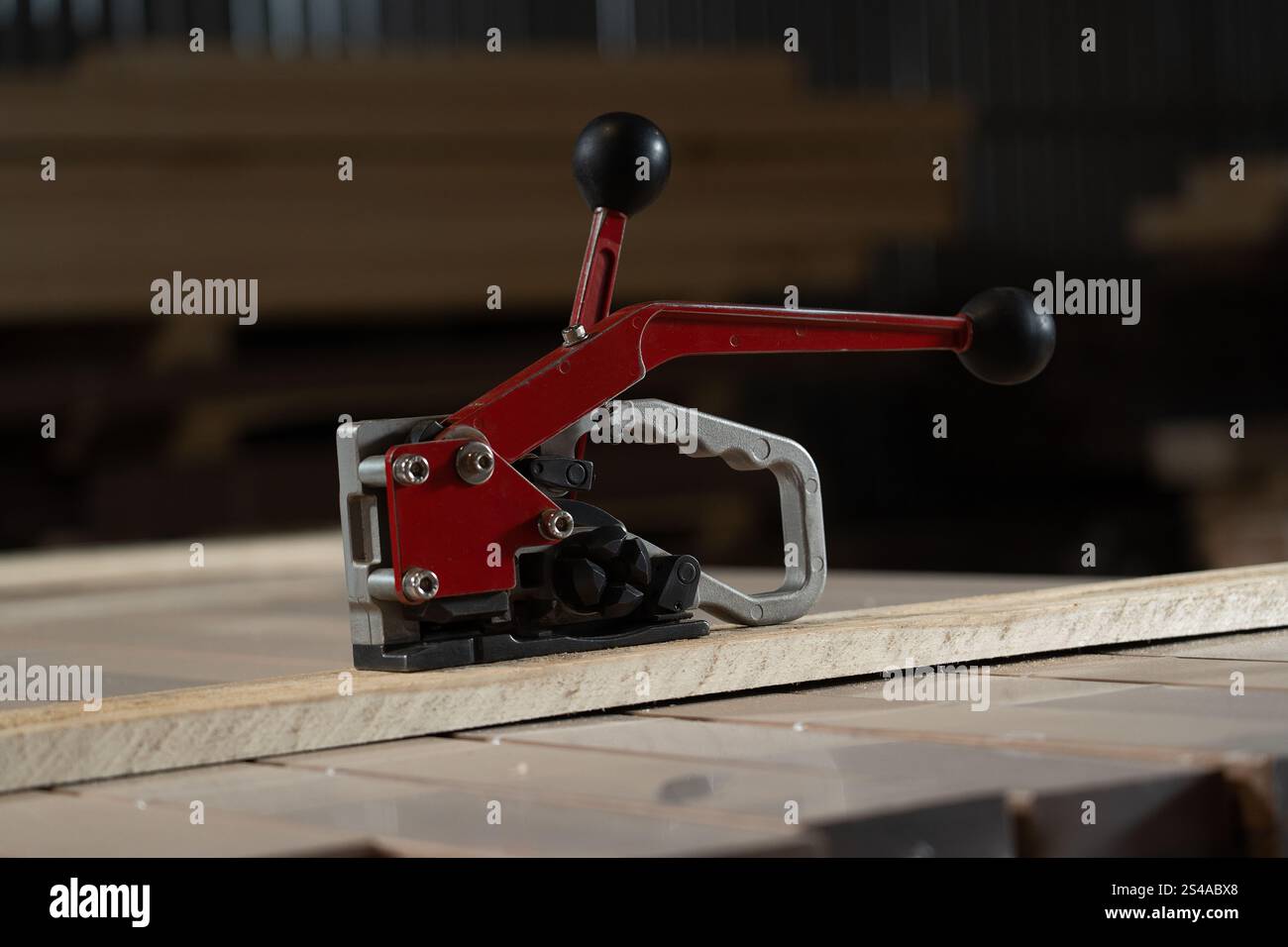 A tie-down tool sits on a stack of wooden planks in the workshop. The ...