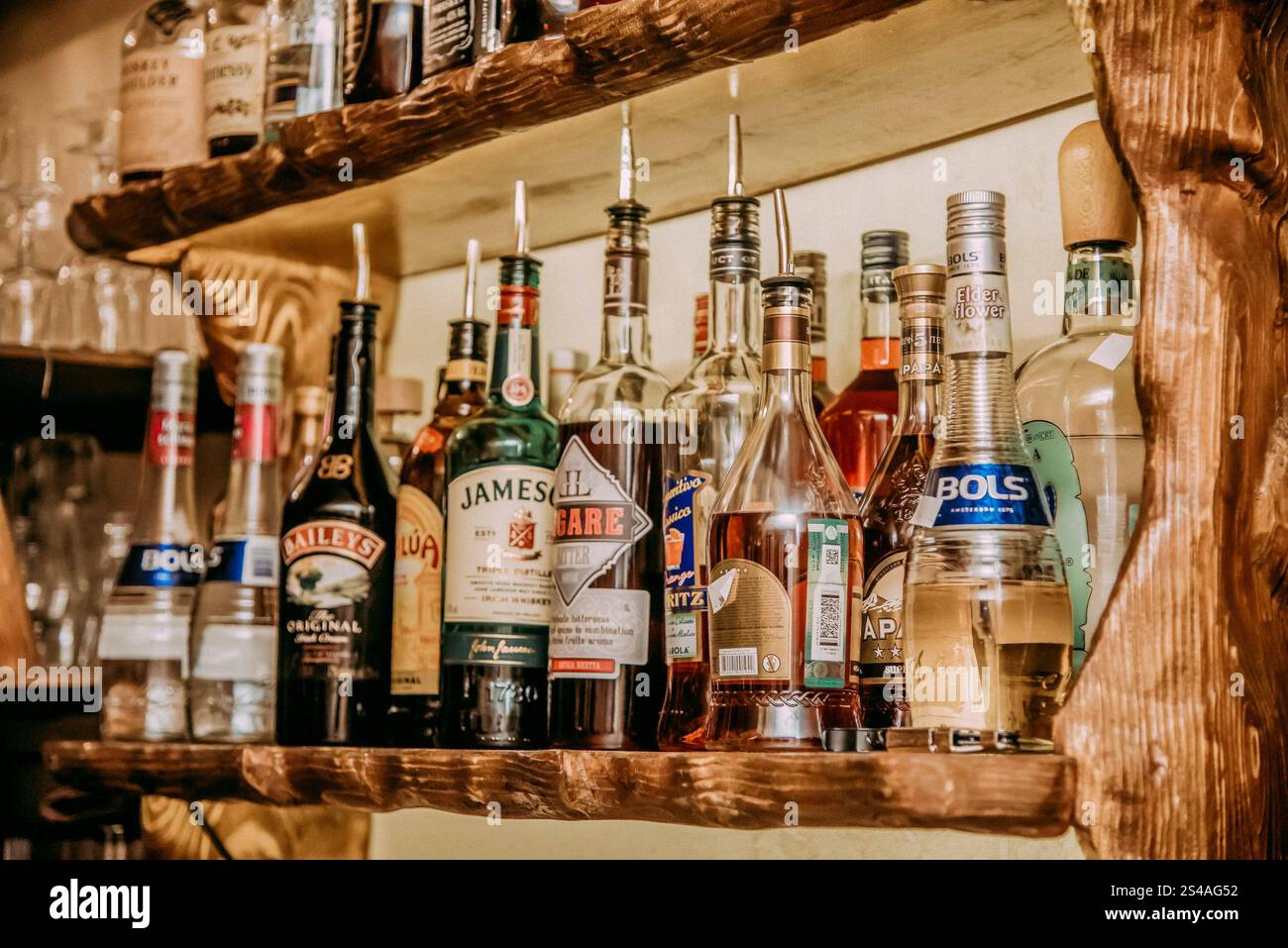 Various glass bottles with alcoholic beverages are on the bar shelf ...