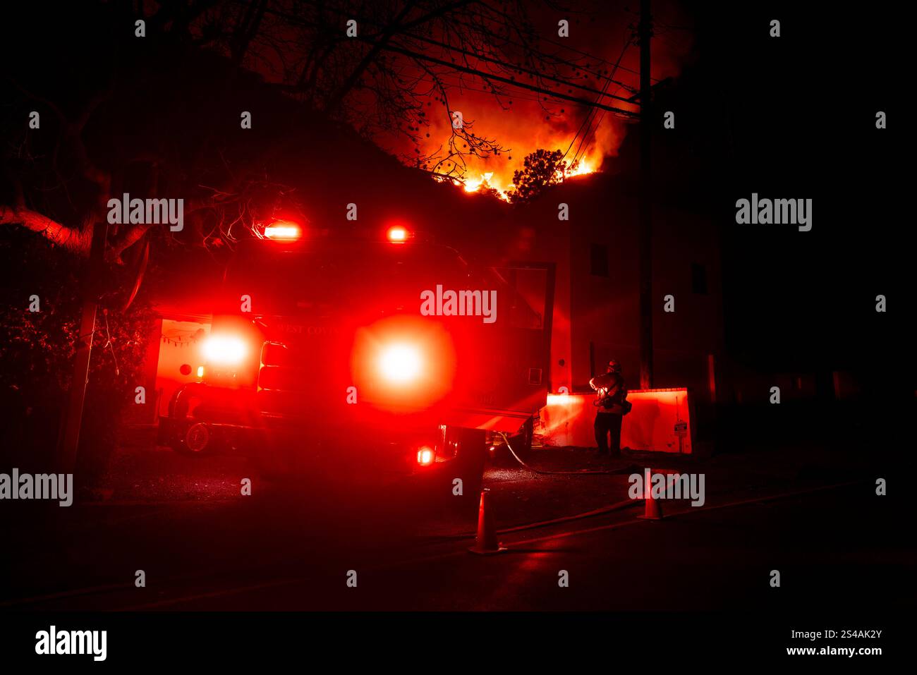 A firefighter sets up to defend houses threatened by the Palisades Fire ...