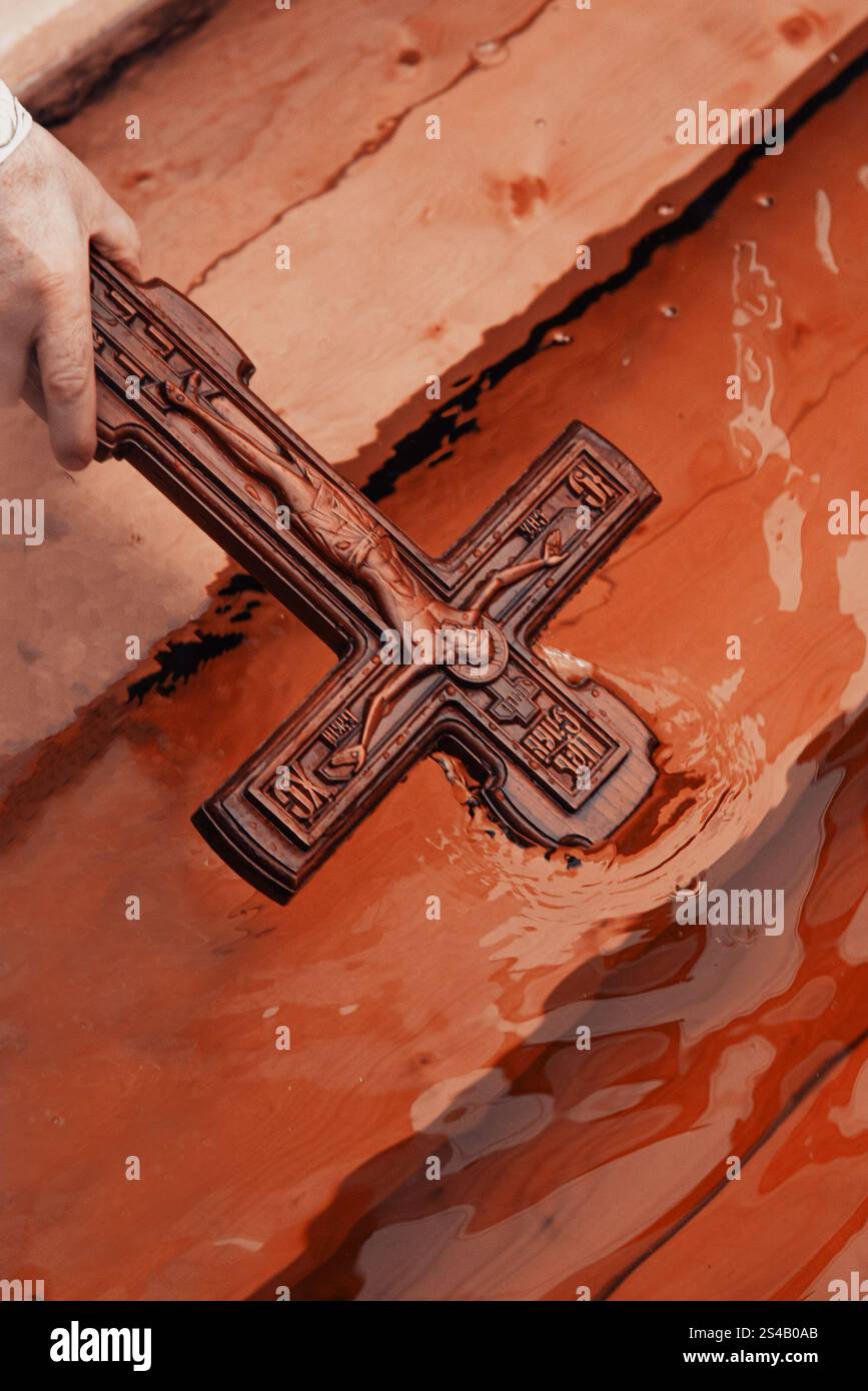 Priest consecrating river water for baptism, holy father holding cross crucifix in hand close up ...