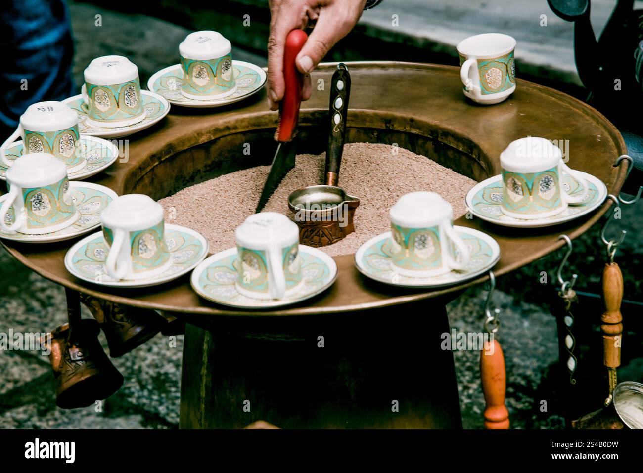 Man prepares Turkish coffee in a traditional way in a cezve on the sand ...
