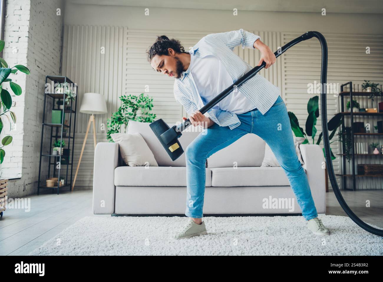 Young man enjoying a creative moment using a vacuum cleaner as a guitar ...