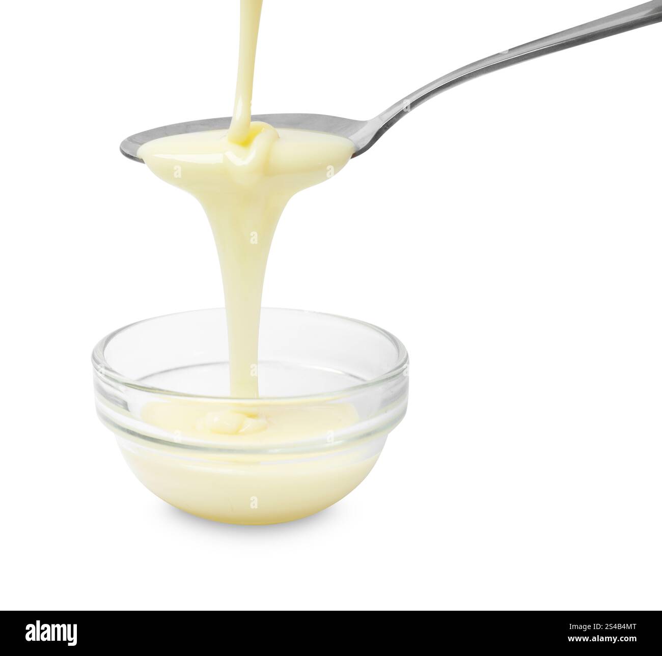 Condensed milk flowing down from spoon into bowl isolated on white ...