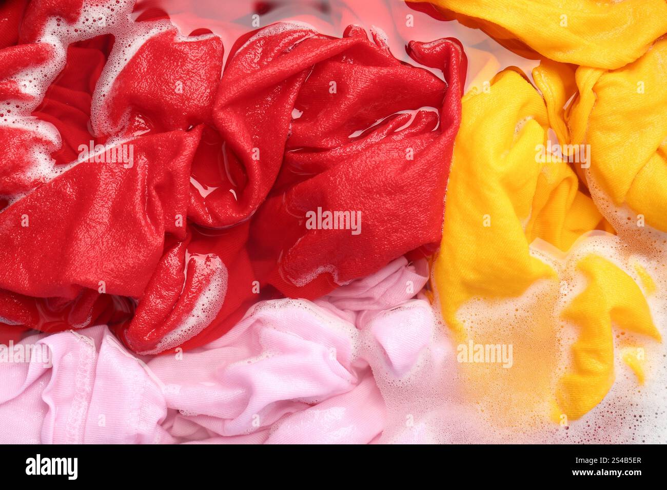 Colorful clothes soaked in water before washing, top view Stock Photo ...