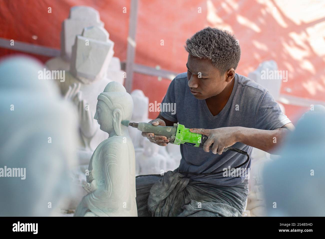 Man making a Buddha statue using an electric sanding machine at a ...