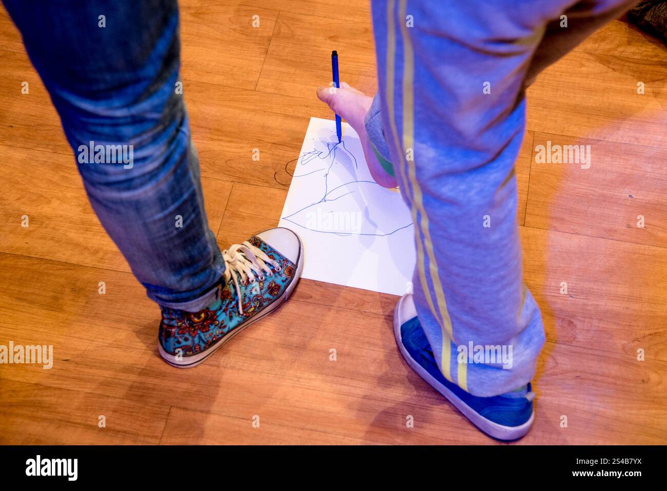 Child draws with his foot with felt tip pen on paper, kid in ...